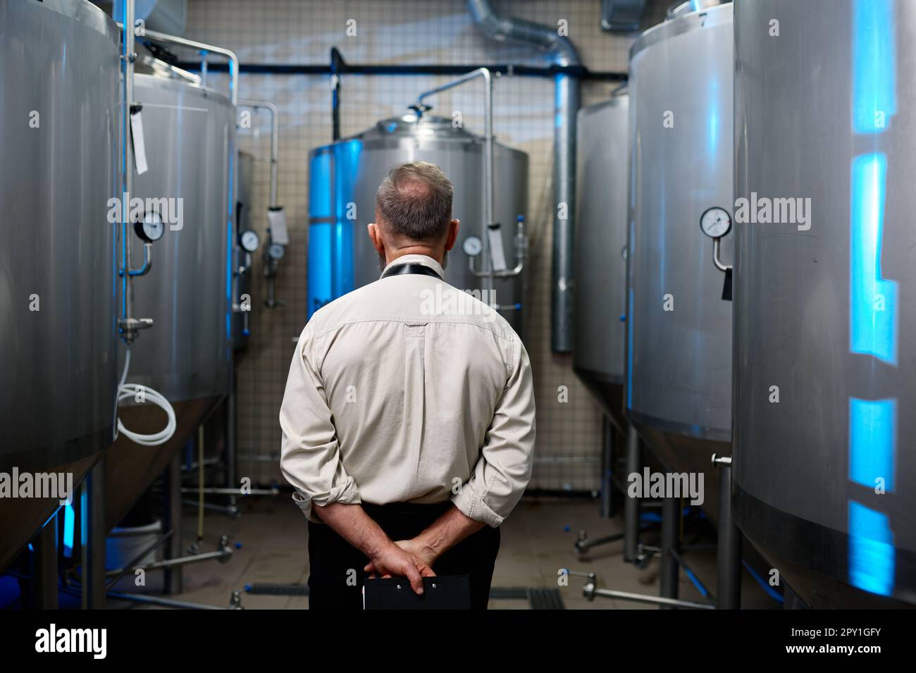 Back view of brewer man in apron standing among distillery vats at beer ...