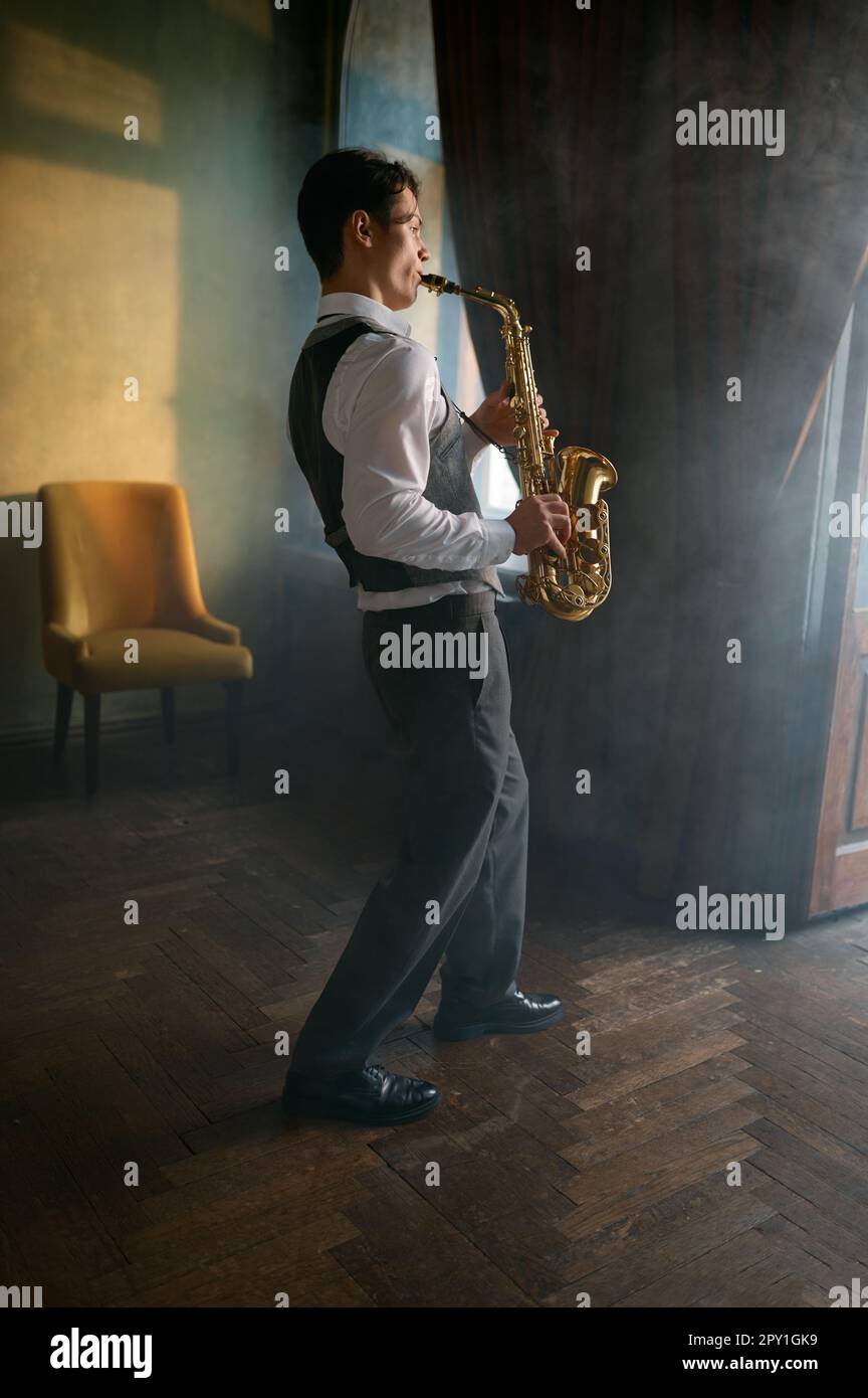 Young elegant man playing gold alto saxophone in misty room. Emotional ...