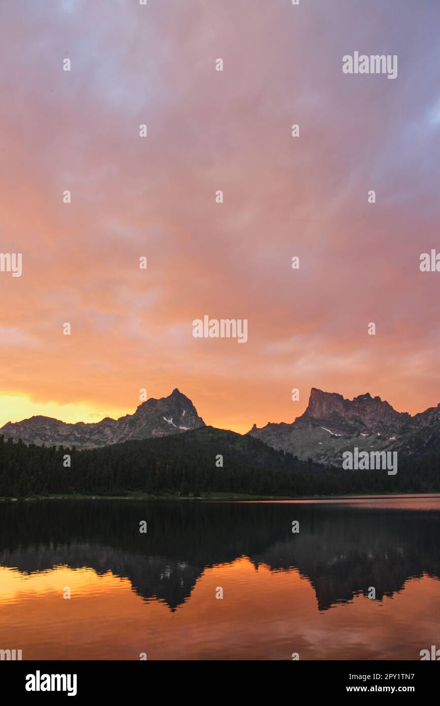 Golden sunset in mountain lake. Two peaks reflected in water. Summer ...