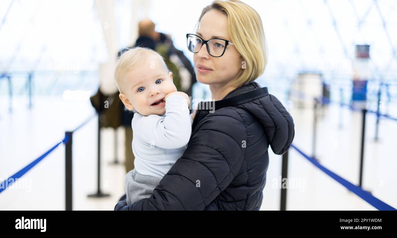 Mother holding his infant baby boy child queuing at airport terminal in ...