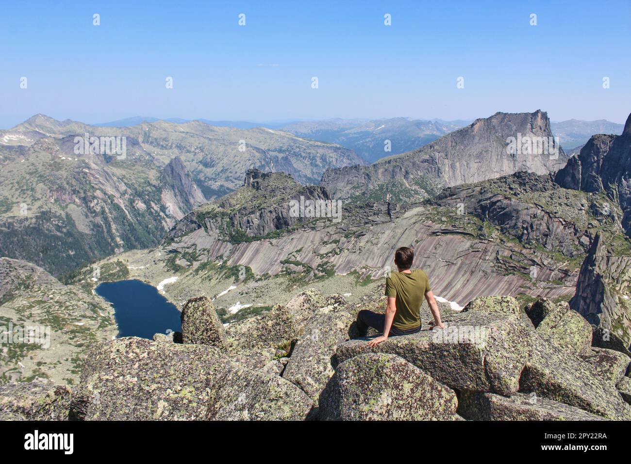 Man tourist sits on a rock high in the mountains. Panoramic view of a ...