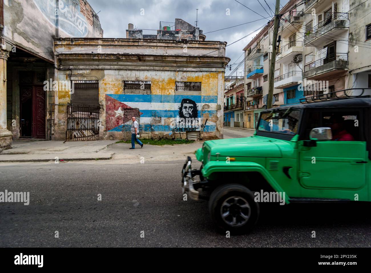 A green jeep moving through one street in Havana with a Cuban flag and ...