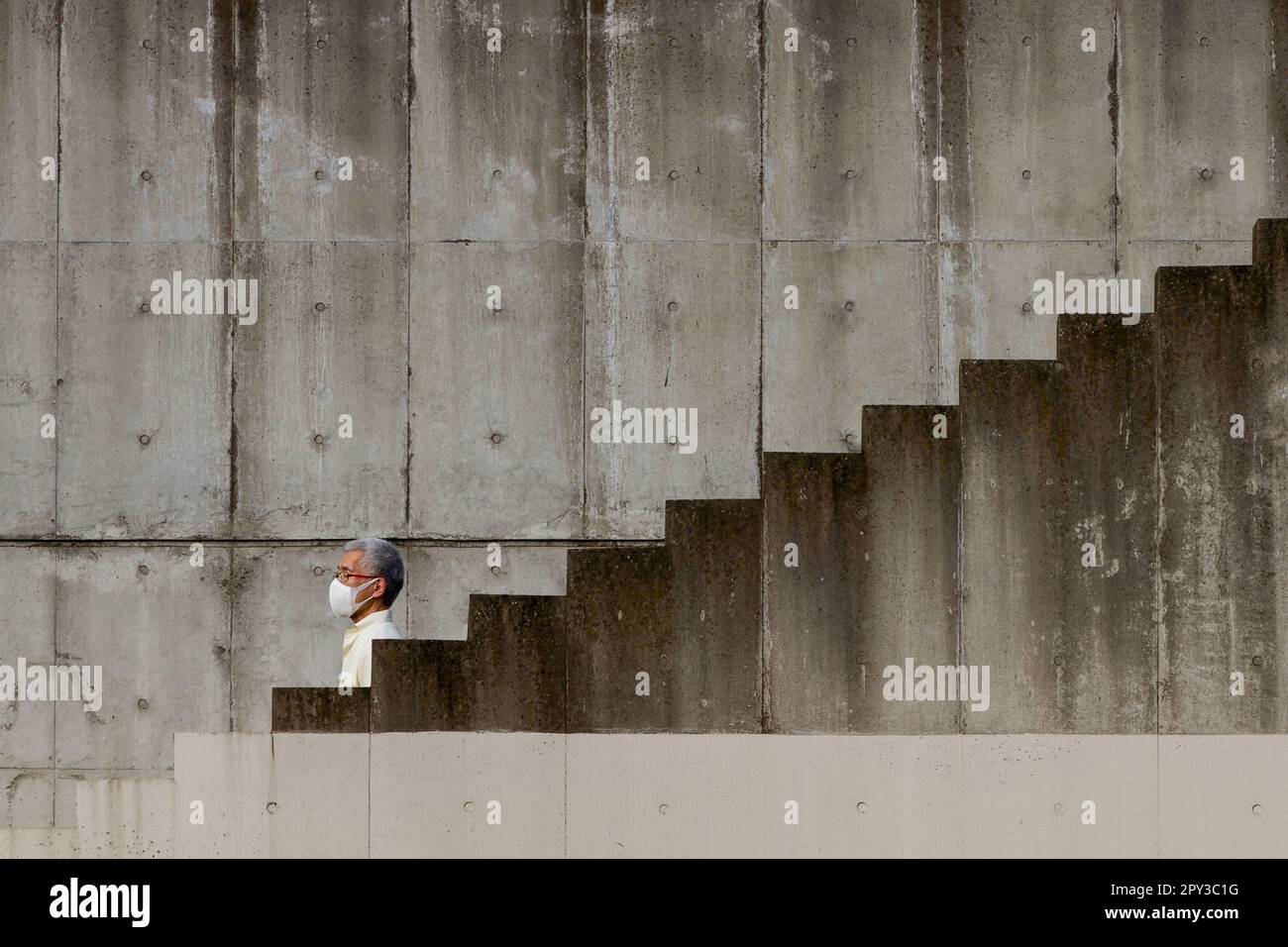 A Japanese man , wearing a surgical face-mask, descends some stairs in ...