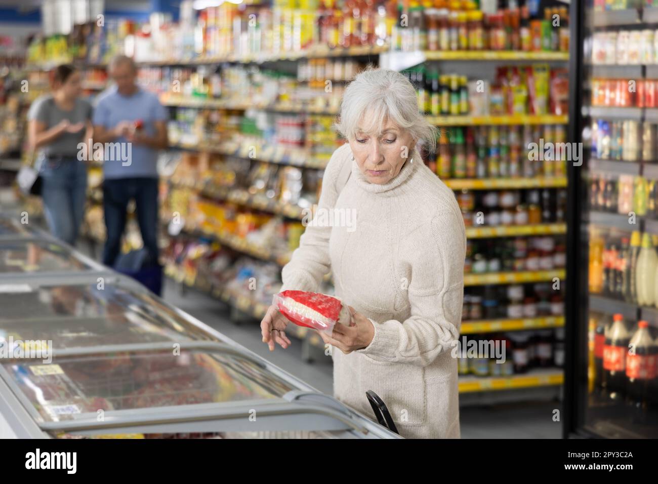 Mature woman choosing frozen food in supermarket. Young woman ...