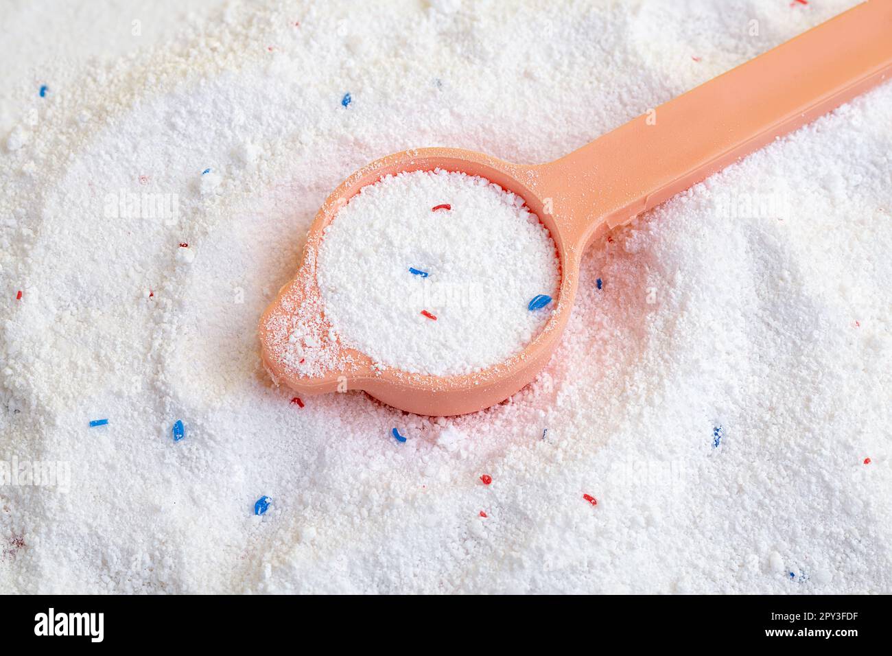 A pile of washing powder and a measuring spoon. Powder with blue and ...