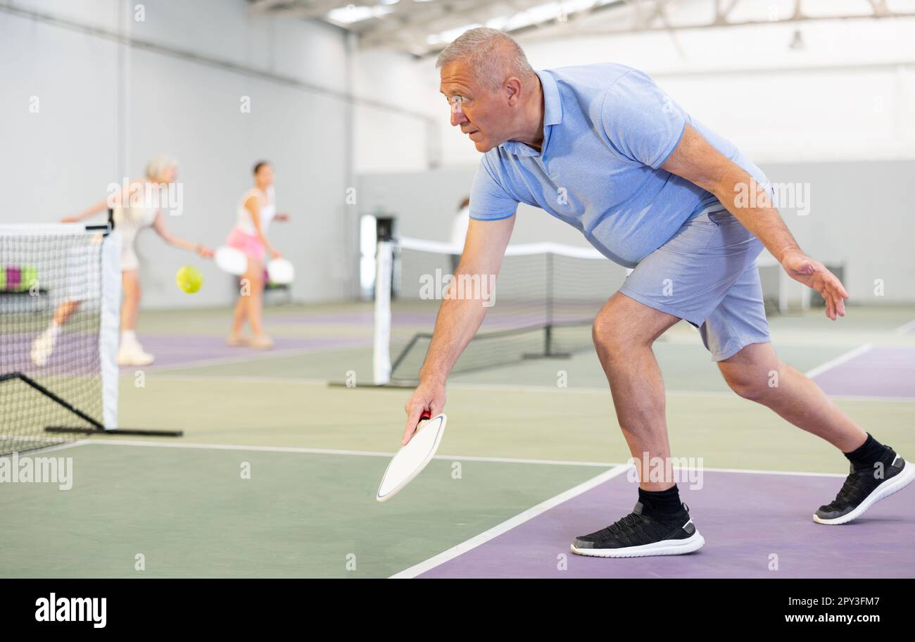 Mature man enjoying popular racket sport pickleball, playing doubles ...