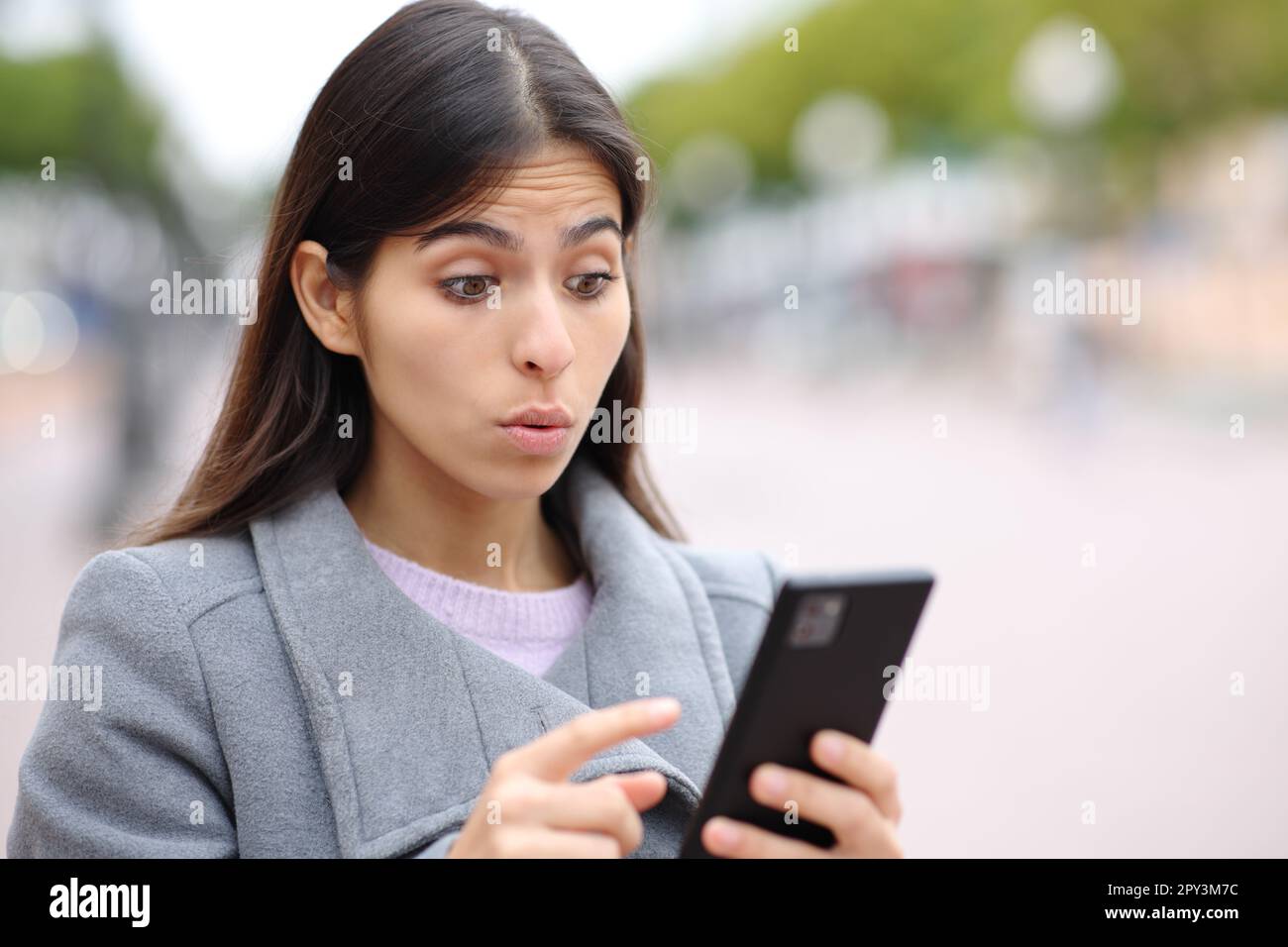 Upset woman saying oops watching phone content in the street in winter ...