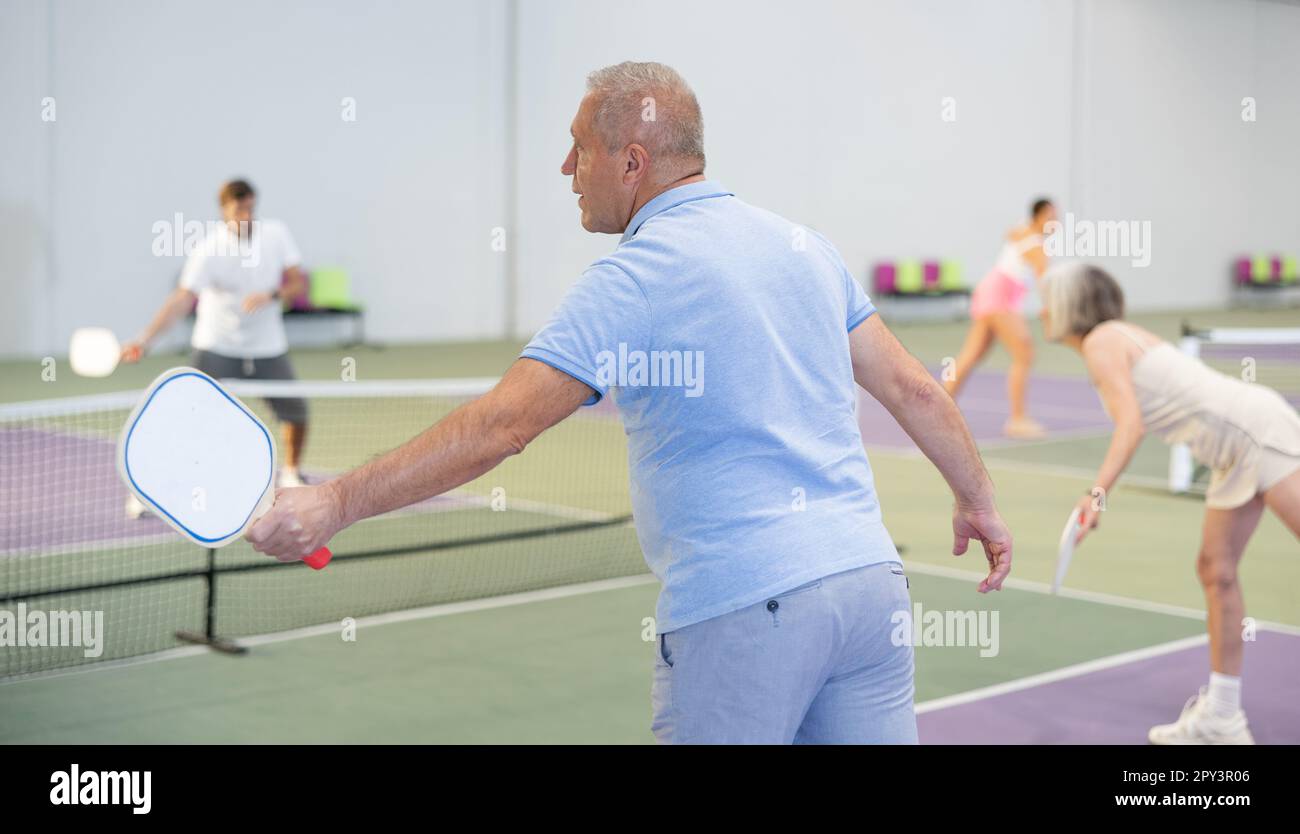Mature man enjoying popular racket sport pickleball, playing doubles ...