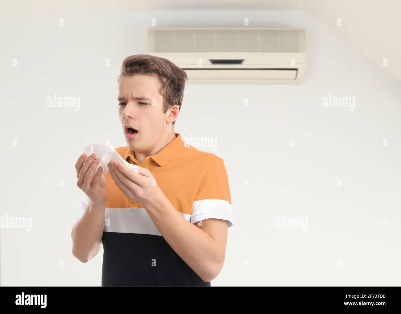 Boy suffering from cold in room with air conditioner on white wall ...