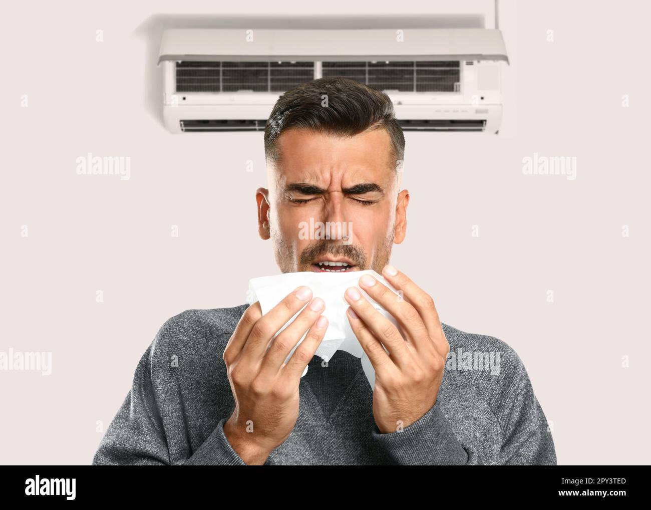 Man suffering from cold in room with air conditioner on white wall ...