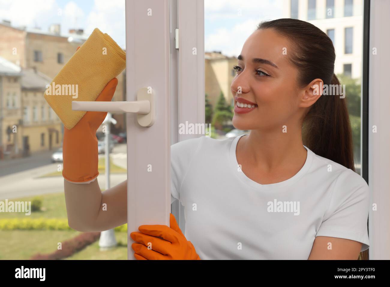 Happy young woman cleaning window glass with rag at home Stock Photo ...