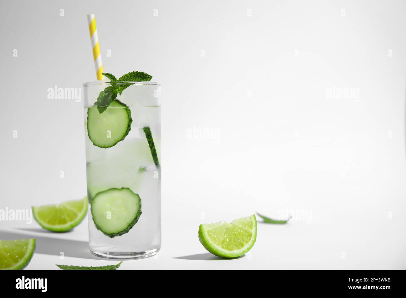 Glass of tasty fresh cucumber water with mint and sliced lime on white background, space for ...