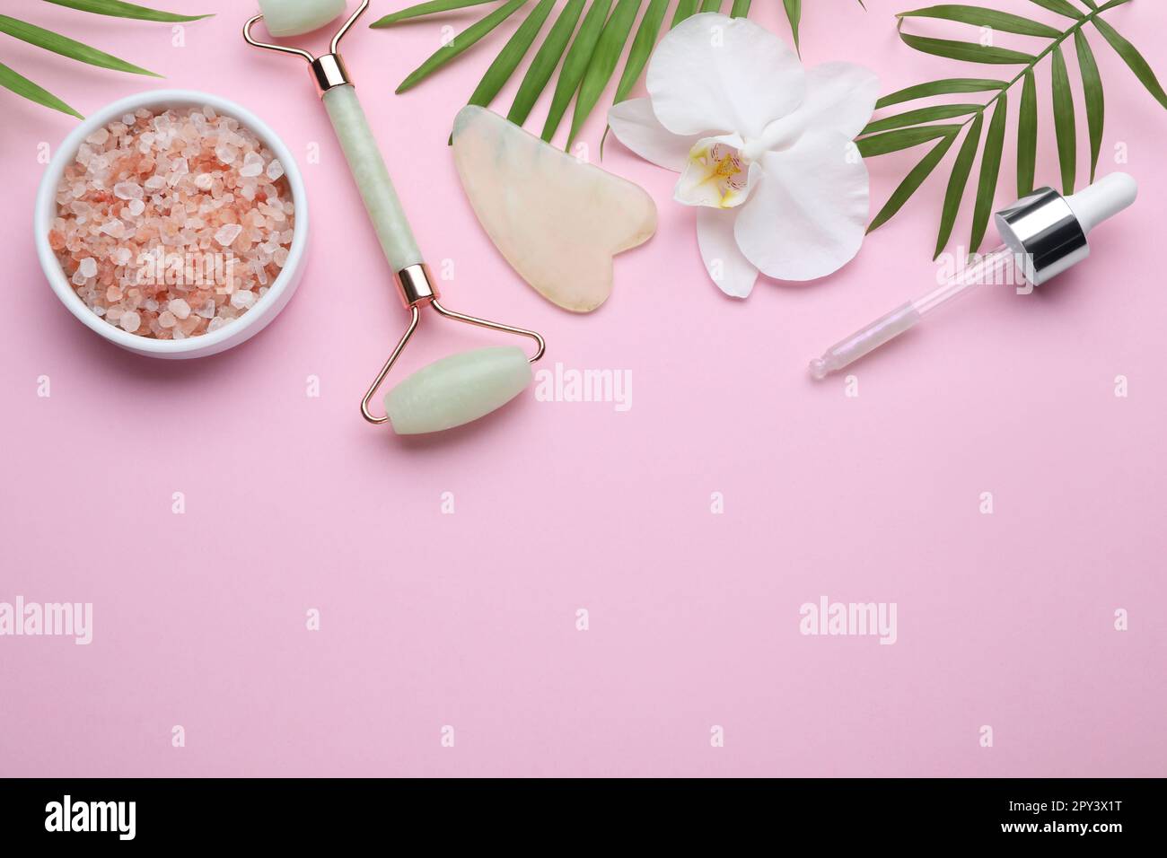 Flat lay composition with gua sha stone and face roller on pink ...