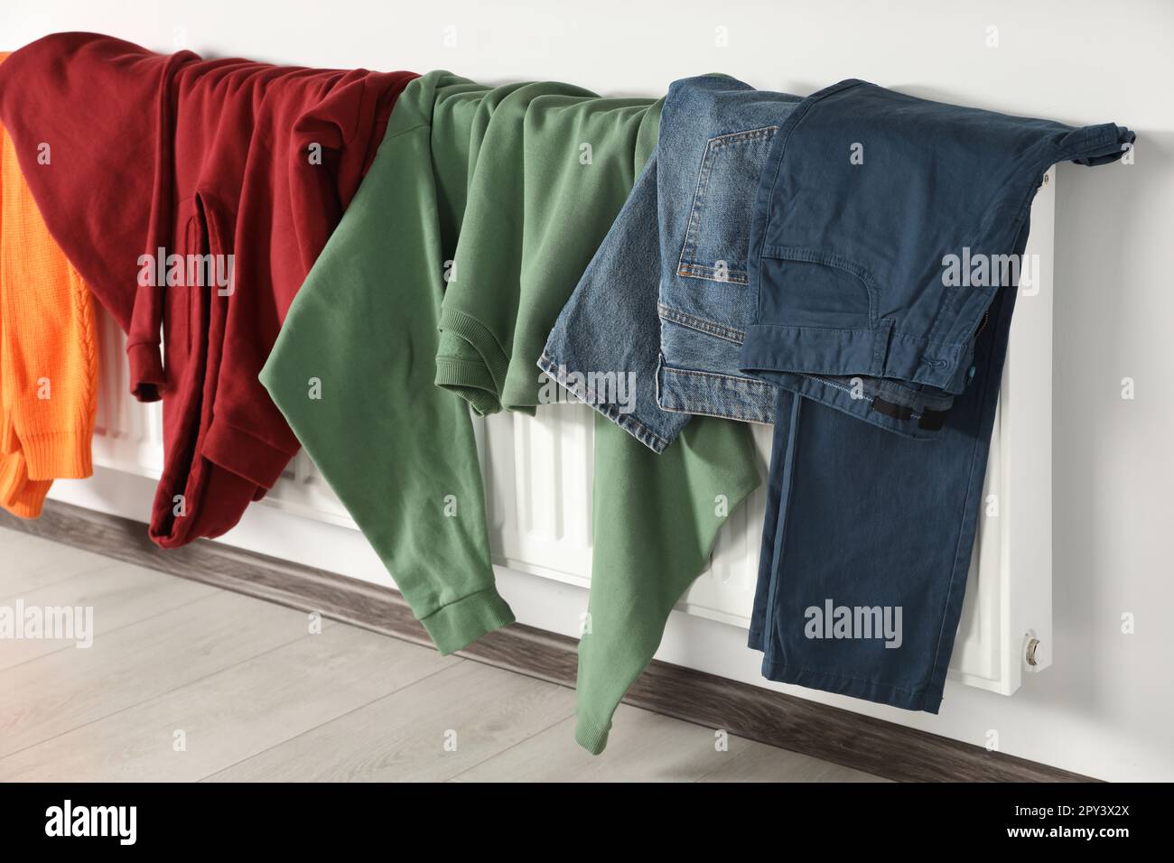 Clean clothes hanging on white radiator indoors Stock Photo - Alamy