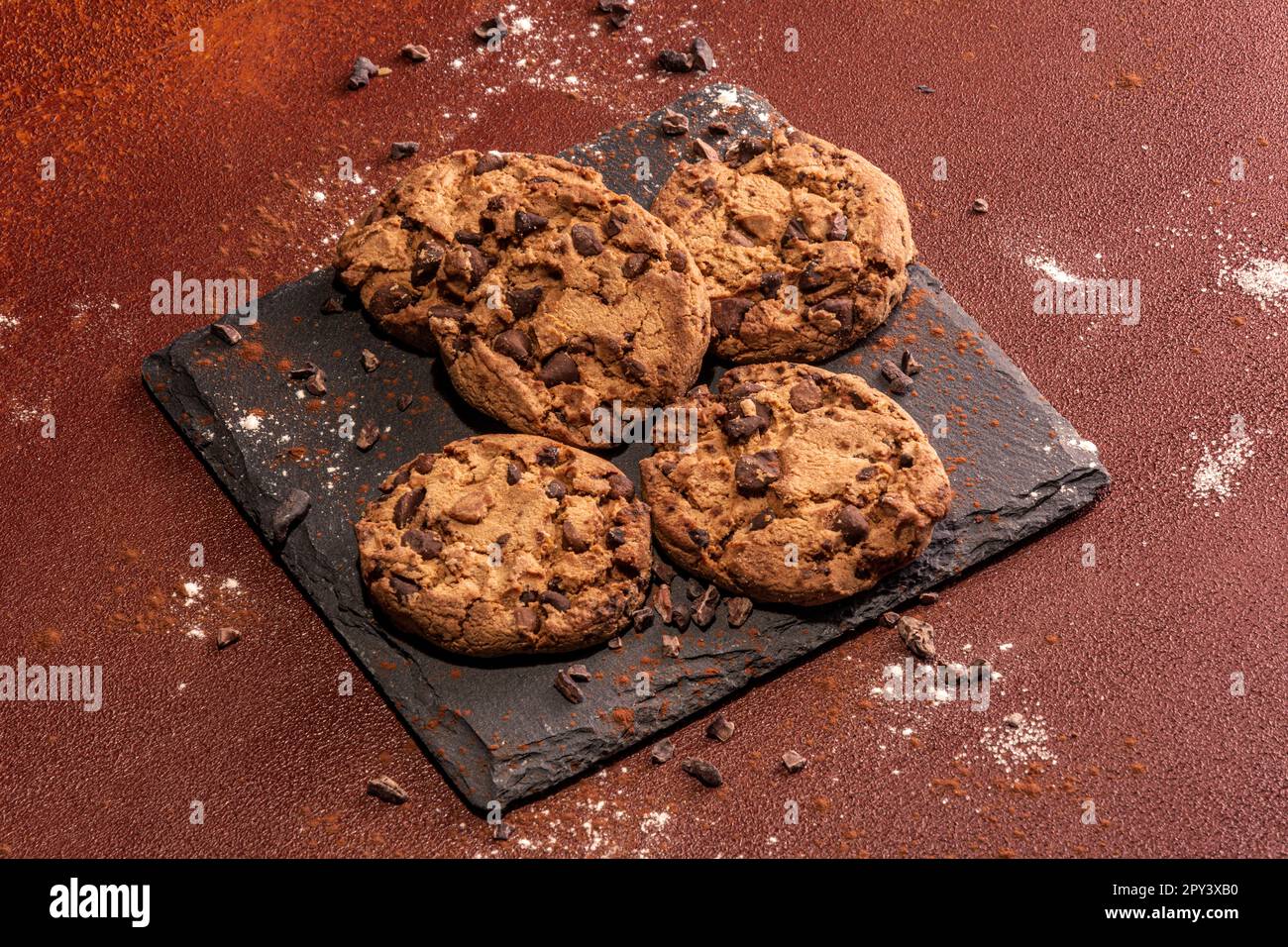 Five cookies with chocolate chips on a slate slab on a brown hand ...
