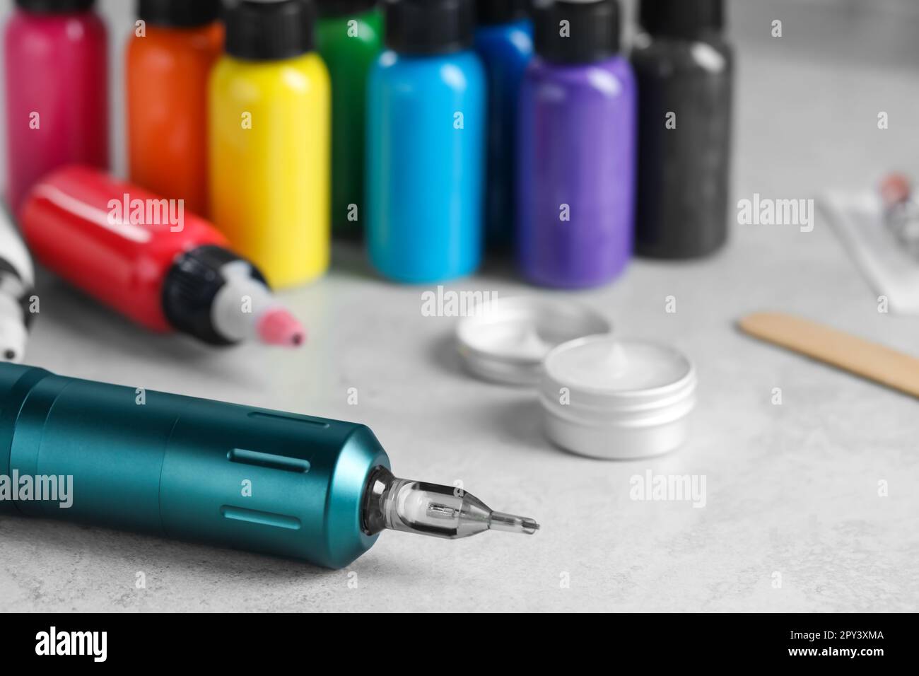 Modern professional tattoo machine and colorful inks on white table ...