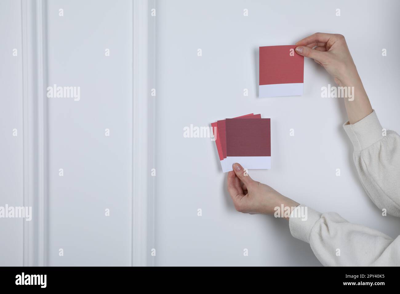 Woman with color sample cards choosing paint shade near white wall ...