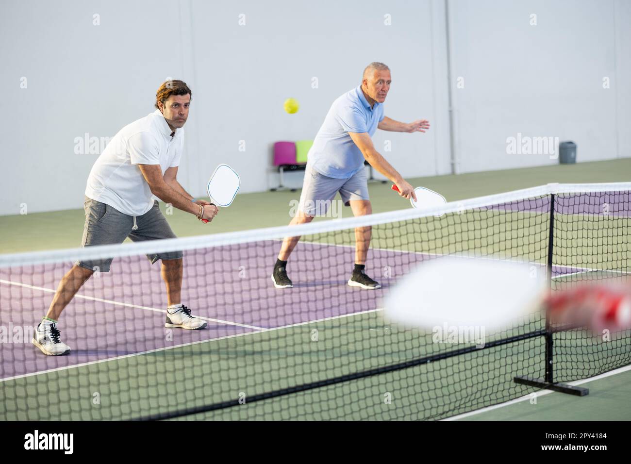 Focused adult man playing pickleball match in team with older partner ...