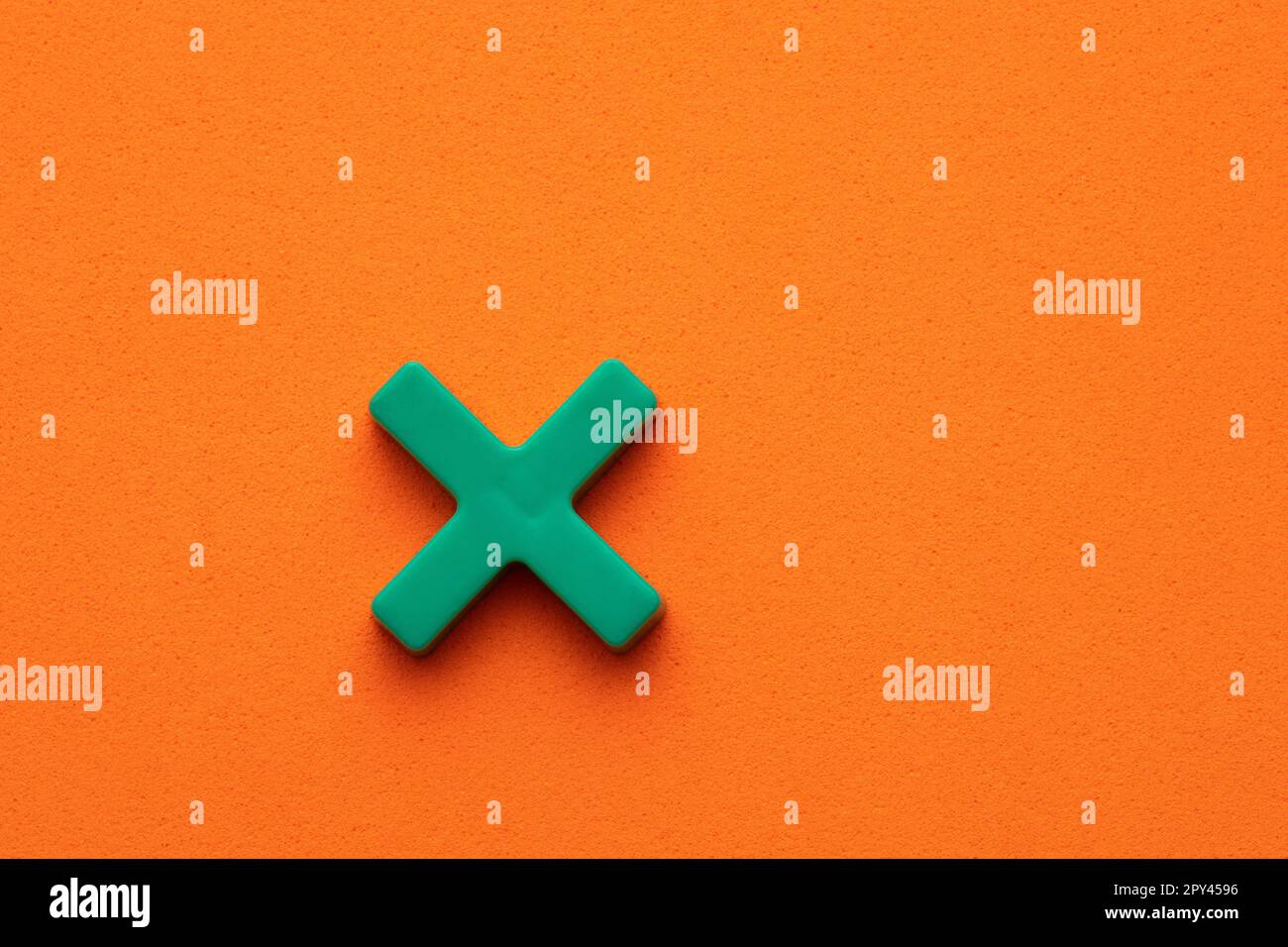 Multiplication sign - Green plastic piece on orange foamy background ...