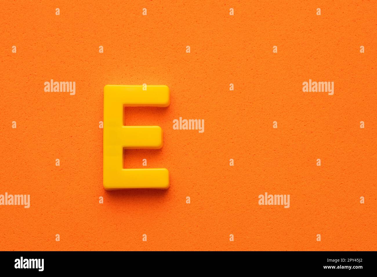 Yellow plastic letter E uppercase on orange foamy background Stock ...