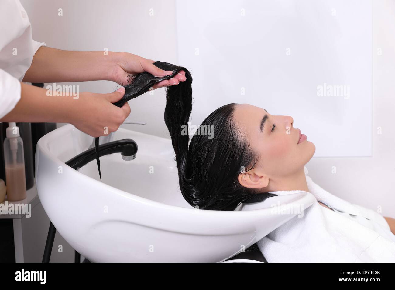 Professional hairdresser applying conditioner on woman's hair in beauty ...
