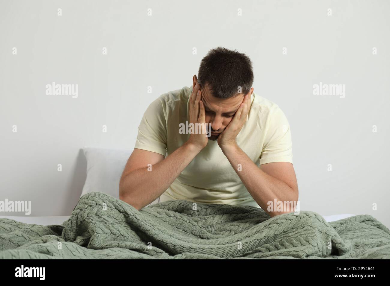 Sleep deprived man sitting on bed at home Stock Photo - Alamy