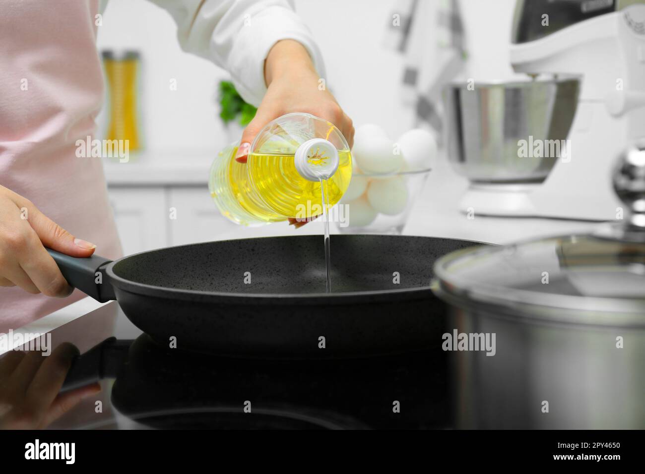 Woman pouring cooking oil from bottle into frying pan in kitchen ...