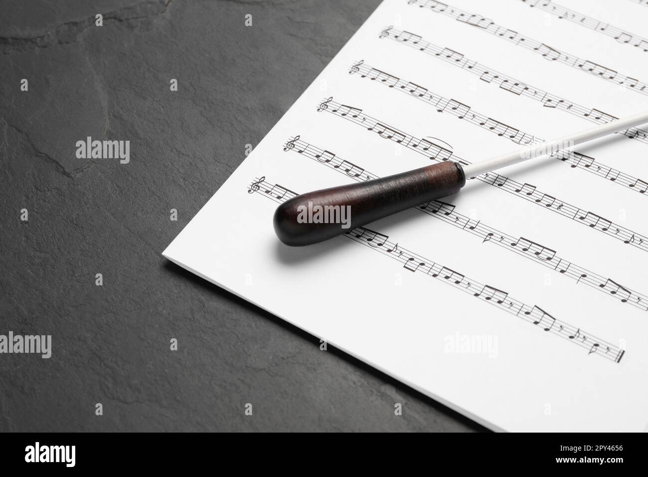 Conductor's baton and sheet music on black background, closeup view ...