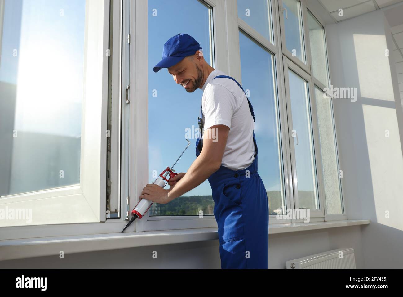 Worker sealing plastic window with caulk indoors. Installation process ...