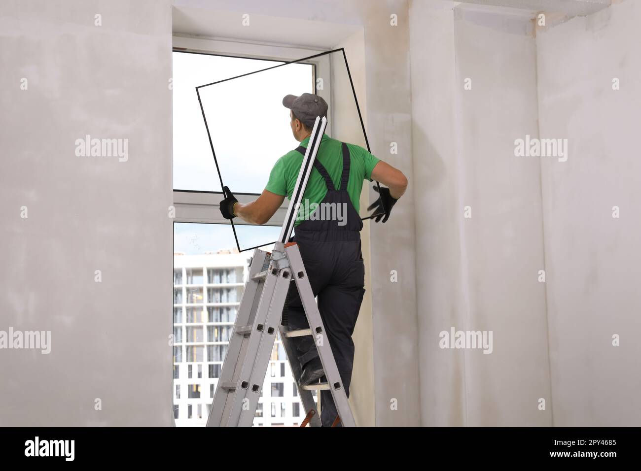 Worker on folding ladder installing window indoors, back view Stock ...