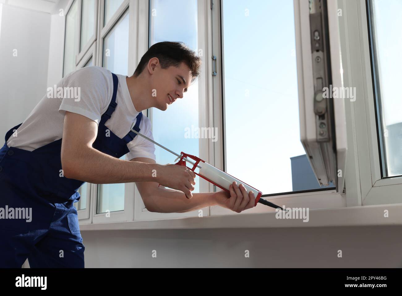 Worker sealing plastic window with caulk indoors. Installation process ...