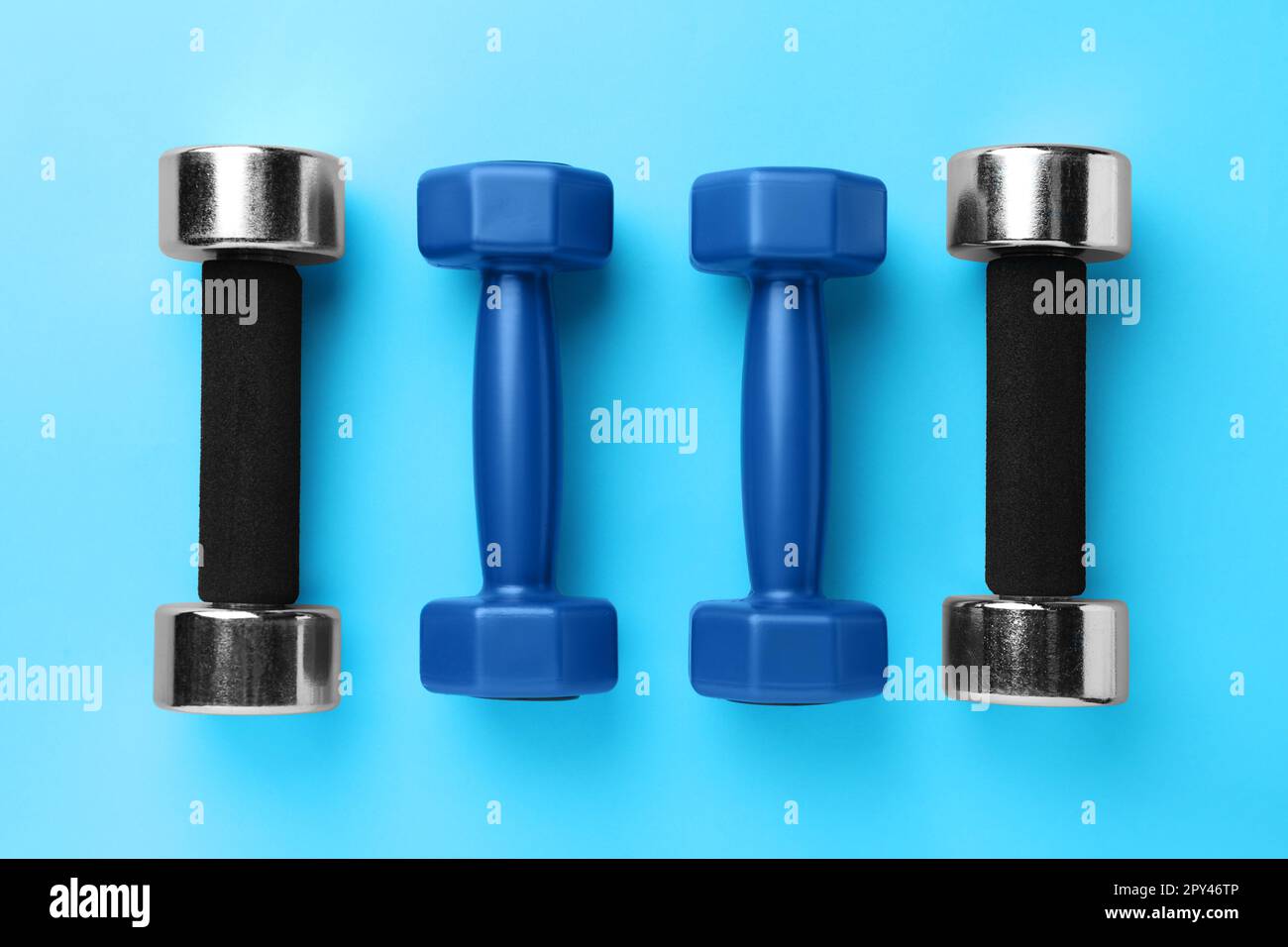 Many different stylish dumbbells on light blue background, flat lay ...