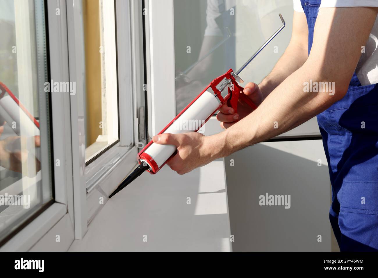 Worker sealing plastic window with caulk indoors, closeup. Installation ...