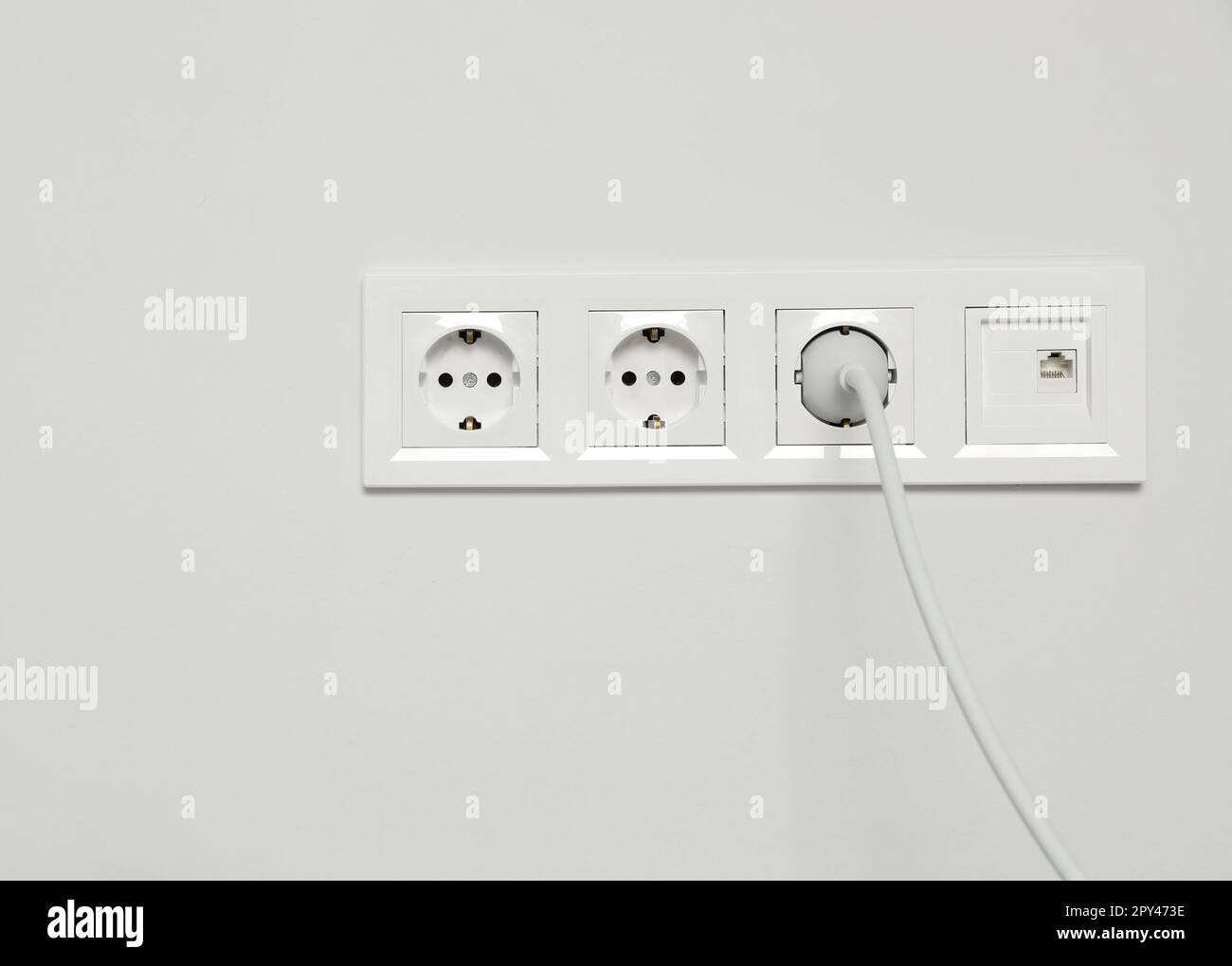 Power sockets with inserted plug on white wall indoors. Electrical ...