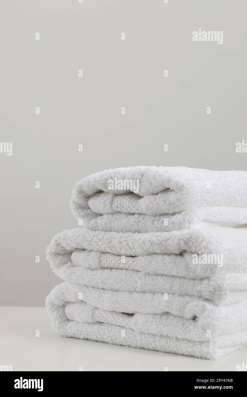 Stack of clean soft white towels on table against light grey background ...