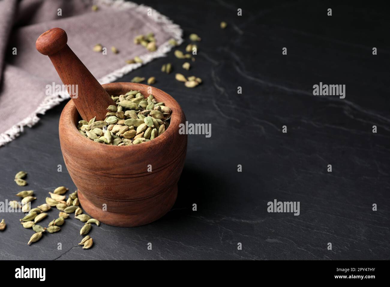 Mortar and pestle with dry cardamom pods on dark grey table, space for ...