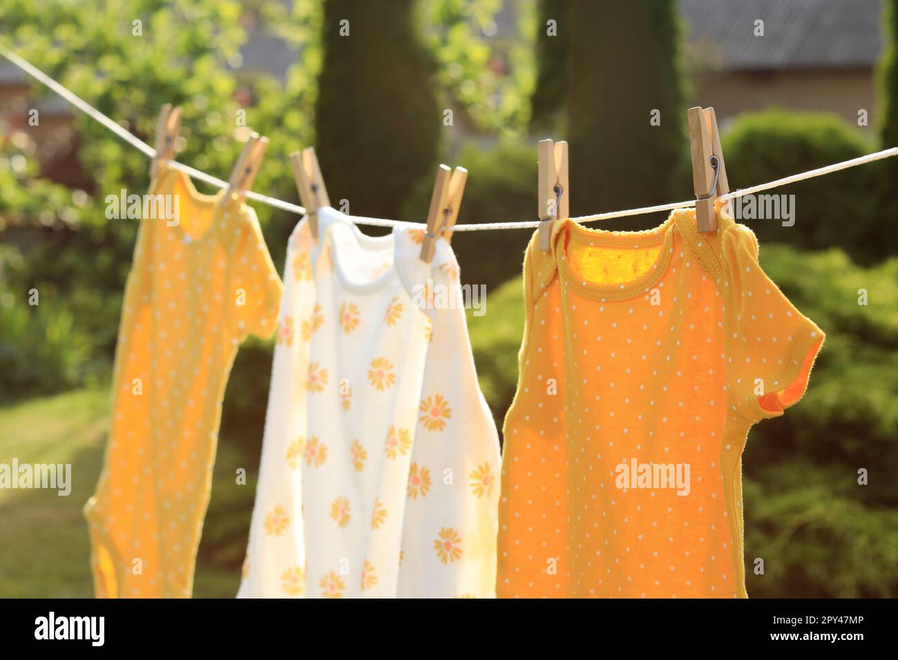 Clean baby onesies hanging on washing line in garden. Drying clothes ...