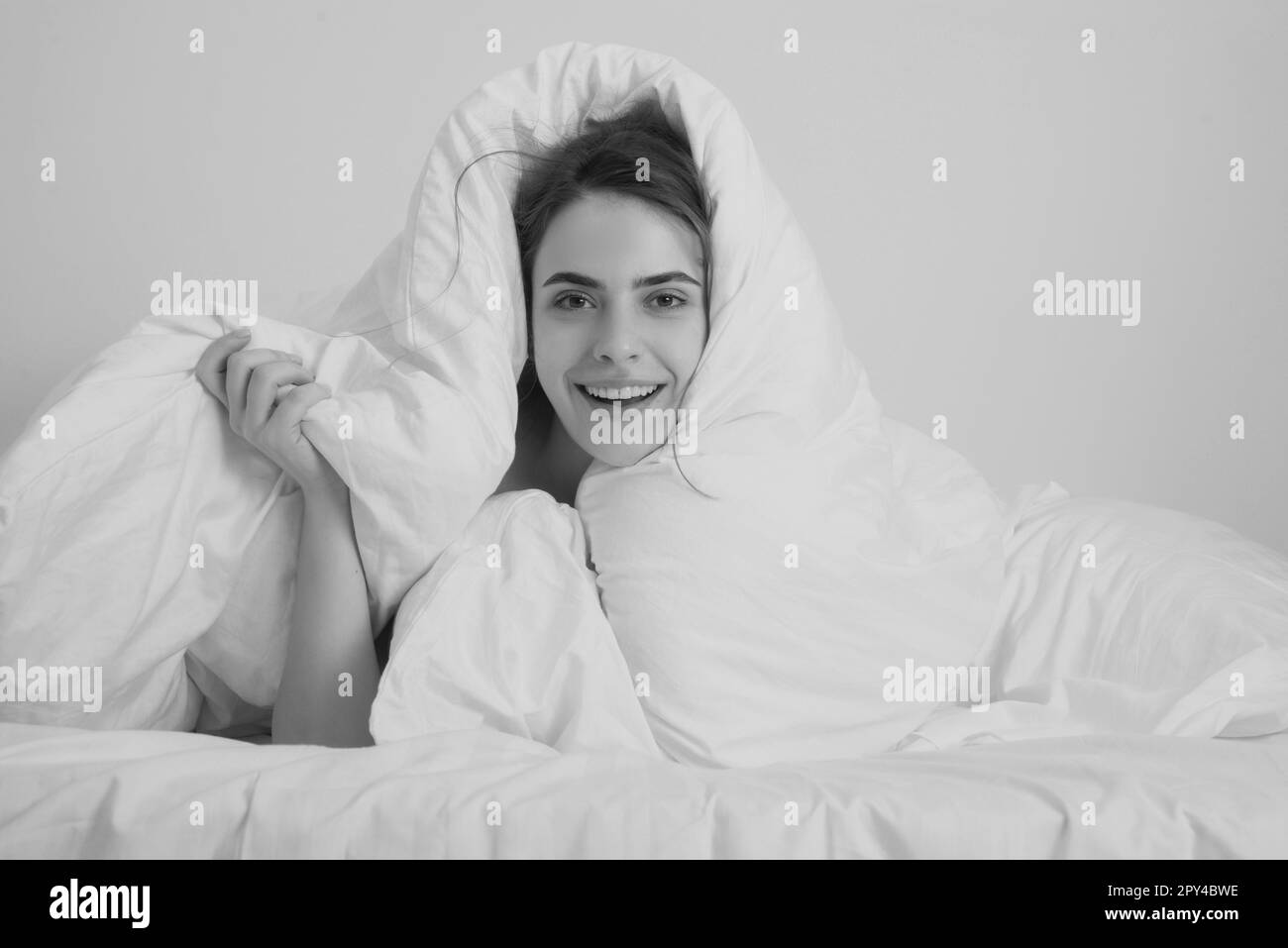 Funny woman with beautiful face is sitting on the bed, wrapped in soft ...