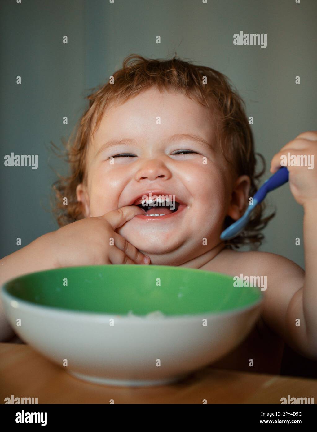 Happy launching baby eating himself with a spoon. Lick tasty fingers ...