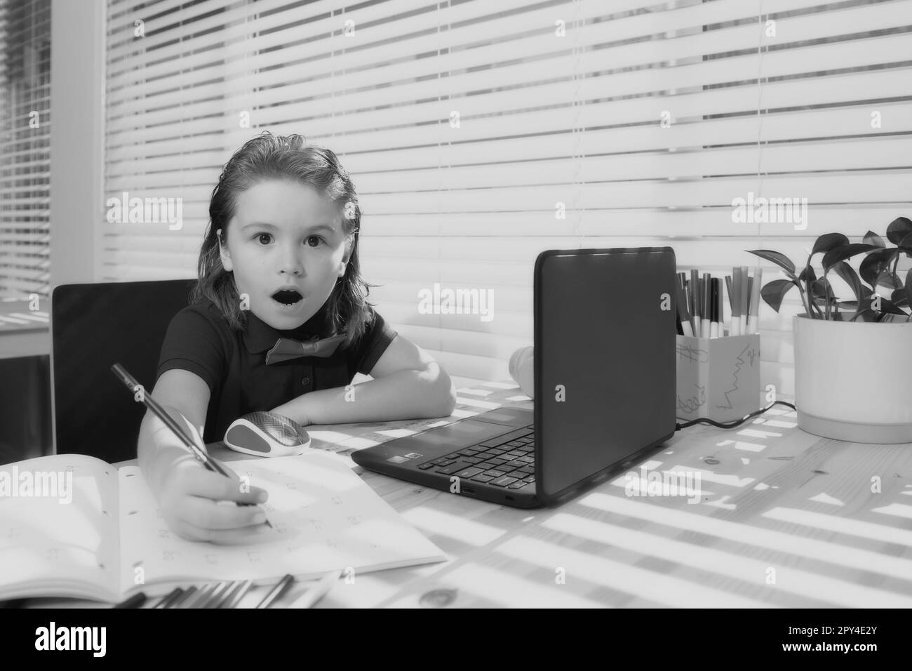 Excited funny schoolboy pupil does homework in school class. Writes ...