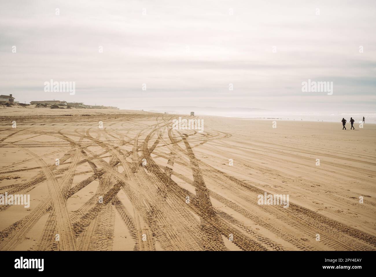 Wide sandy beach, tire tracks, and silhouettes of walking people ...