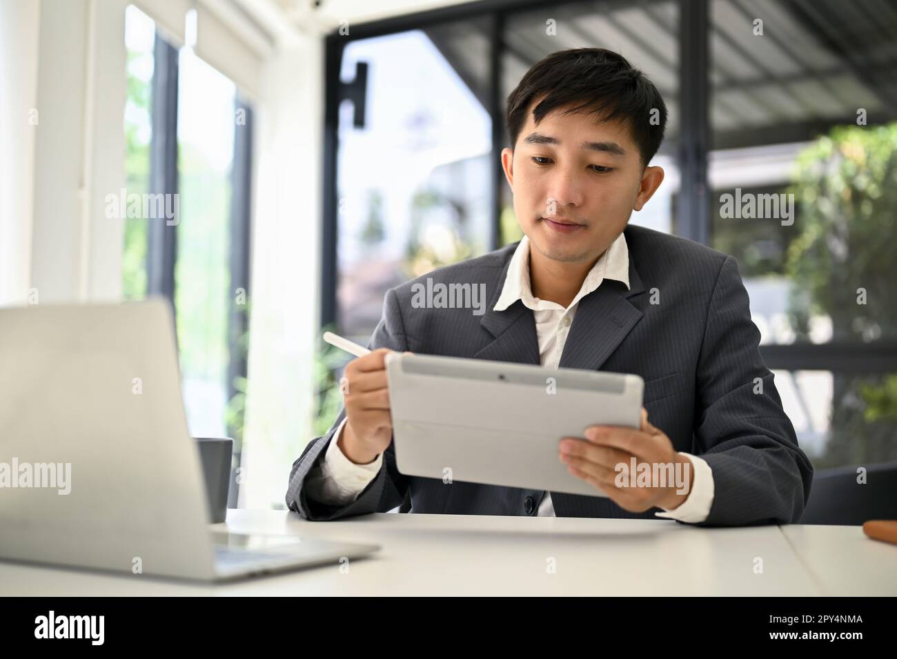 A focused millennial Asian male boss using his digital tablet to manage ...