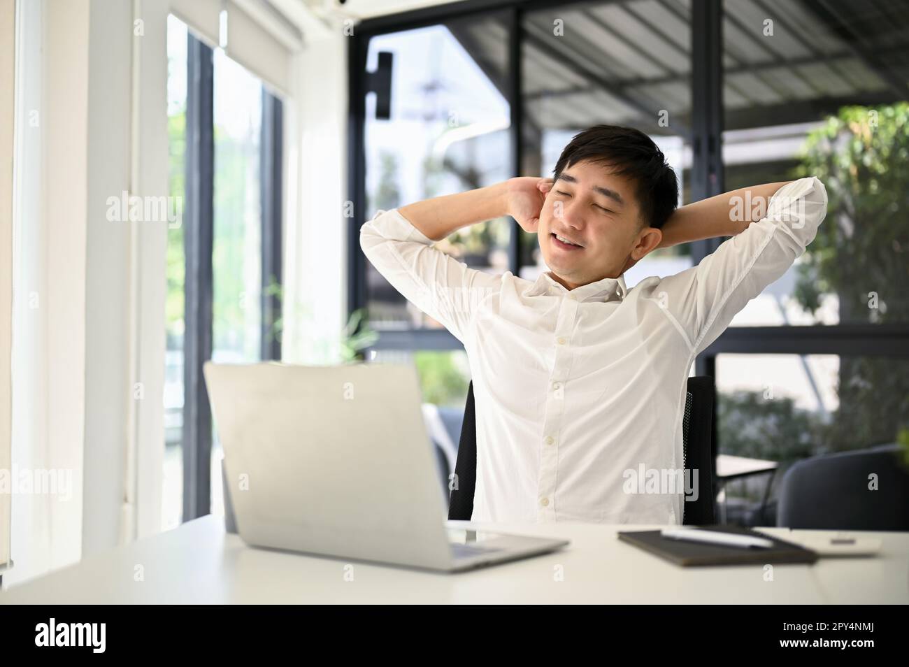 Tired millennial Asian businessman sits at his desk in the office ...