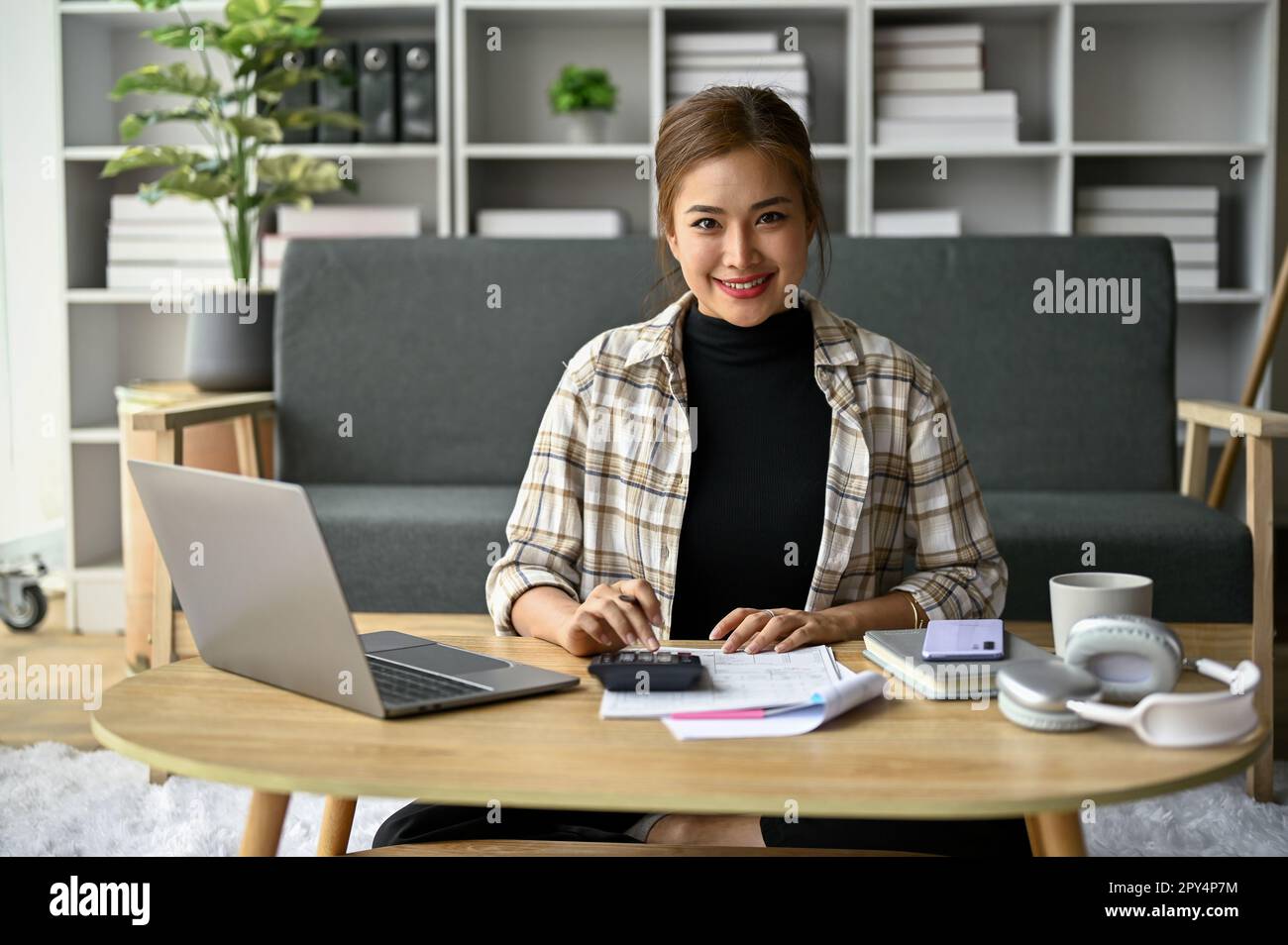 Smiling young Asian woman calculating monthly budget and expenses at a ...