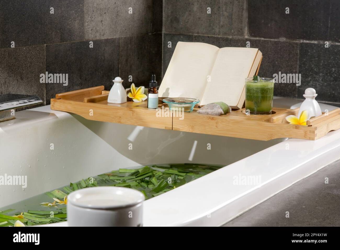 Tub full of water and herbs with wooden bathtub tray with various ...