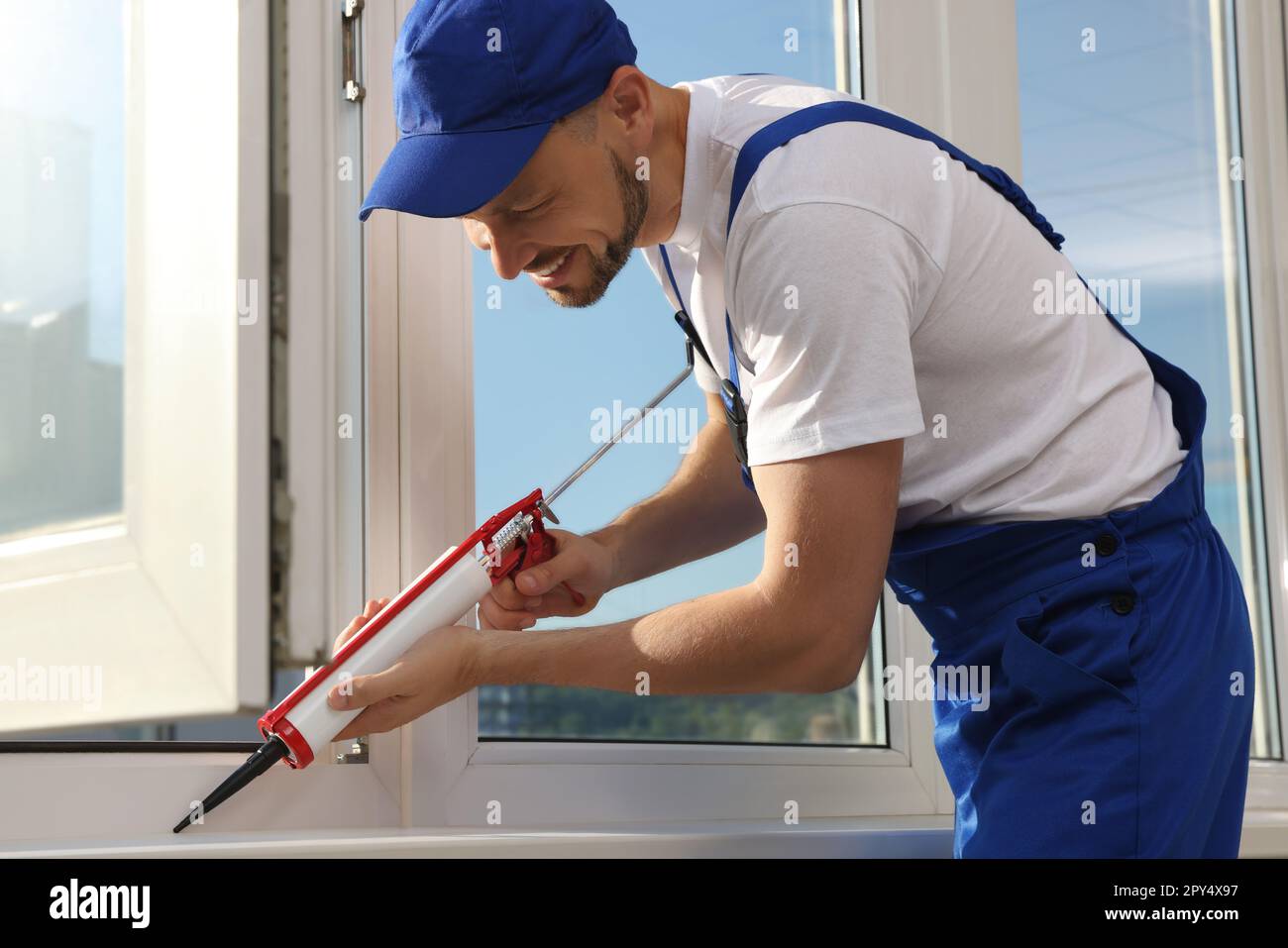 Worker sealing plastic window with caulk indoors. Installation process ...