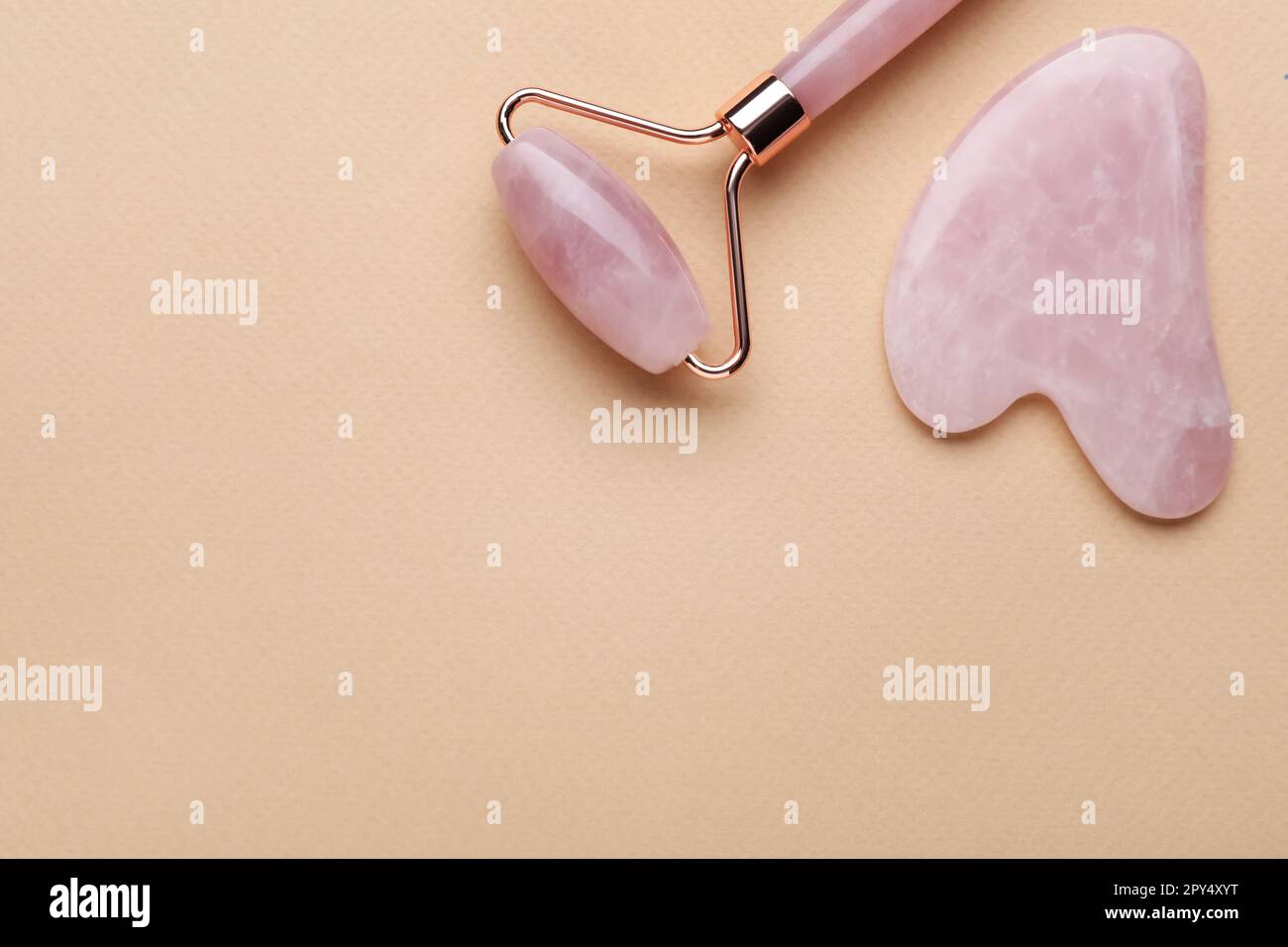 Gua sha stone and face roller on beige background, flat lay. Space for ...