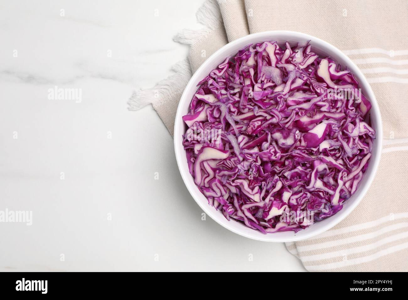 Bowl with shredded red cabbage on white marble table, top view. Space ...