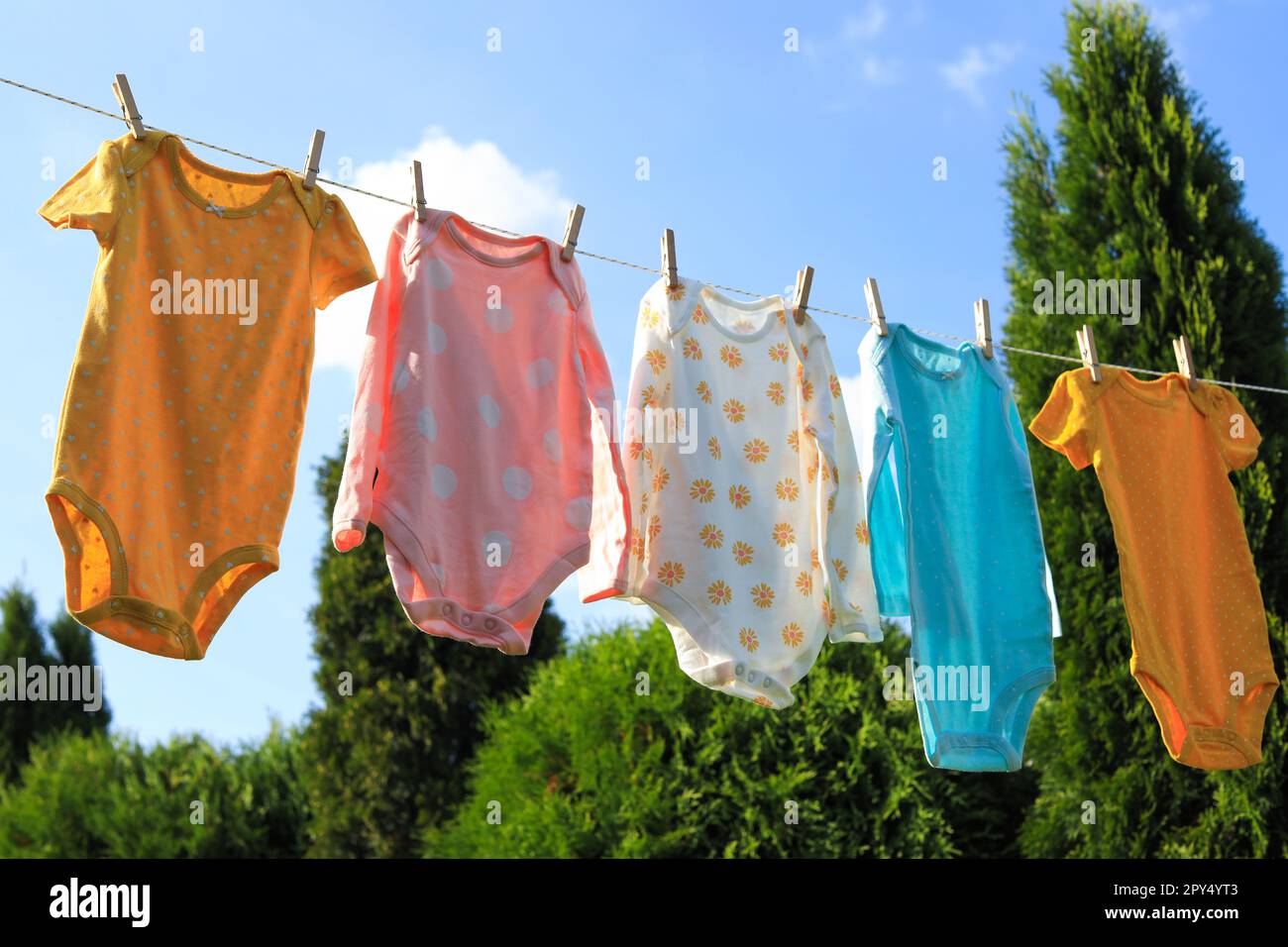 Clean baby onesies hanging on washing line in garden. Drying clothes ...