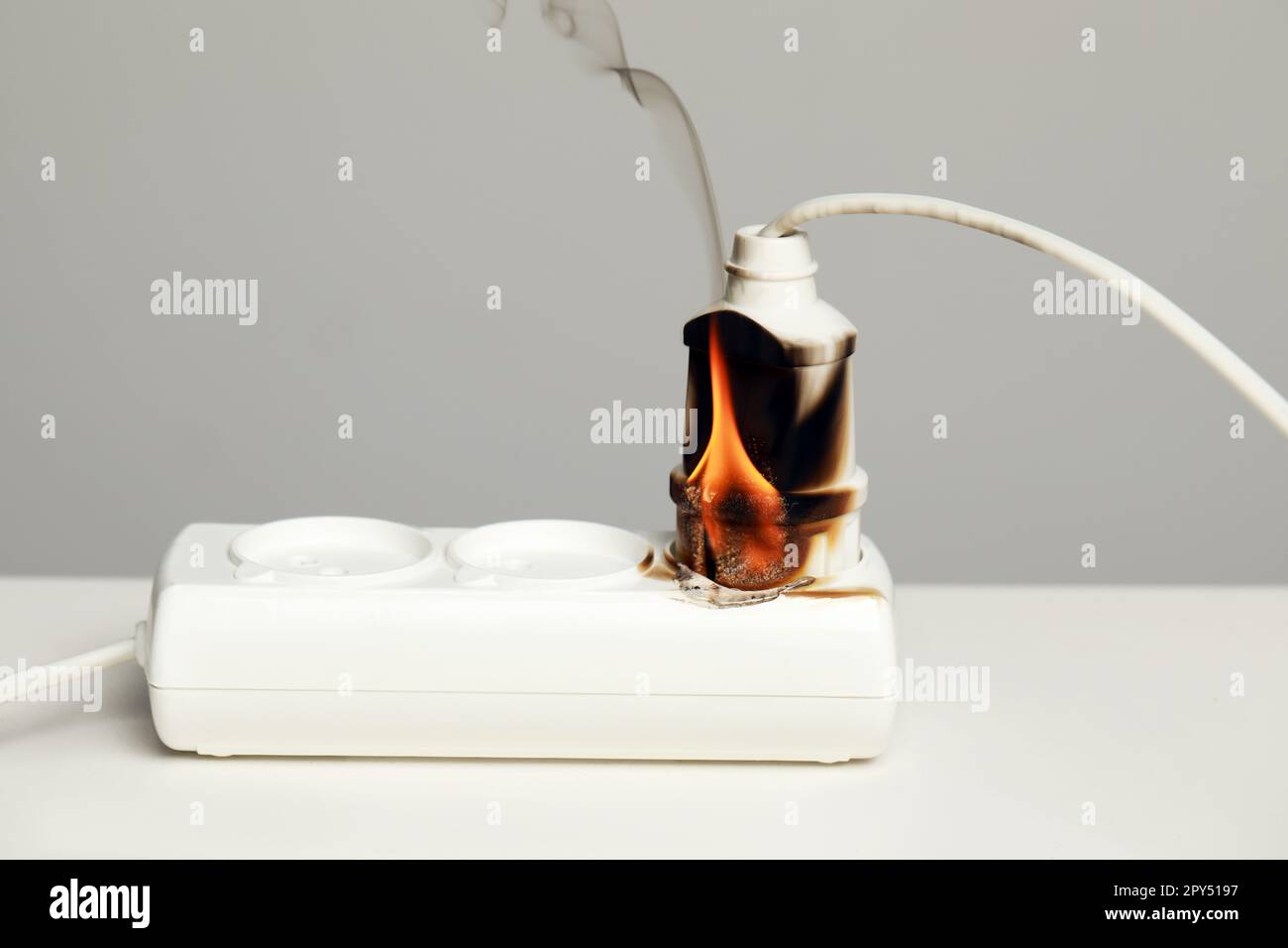 Inflamed plug in power strip on white table against grey wall ...